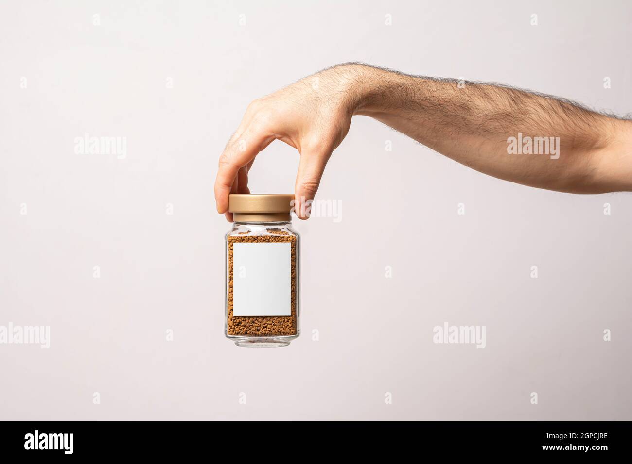 A male hand holding an instant coffee glass jar with blank label ...