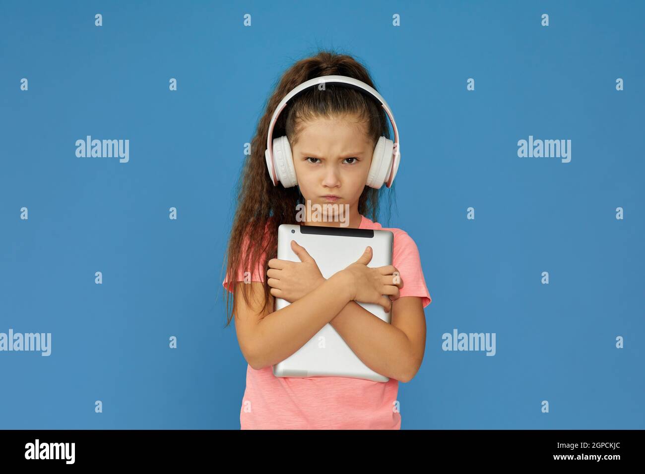 angry little child girl in headphones holding digital tablet and ...