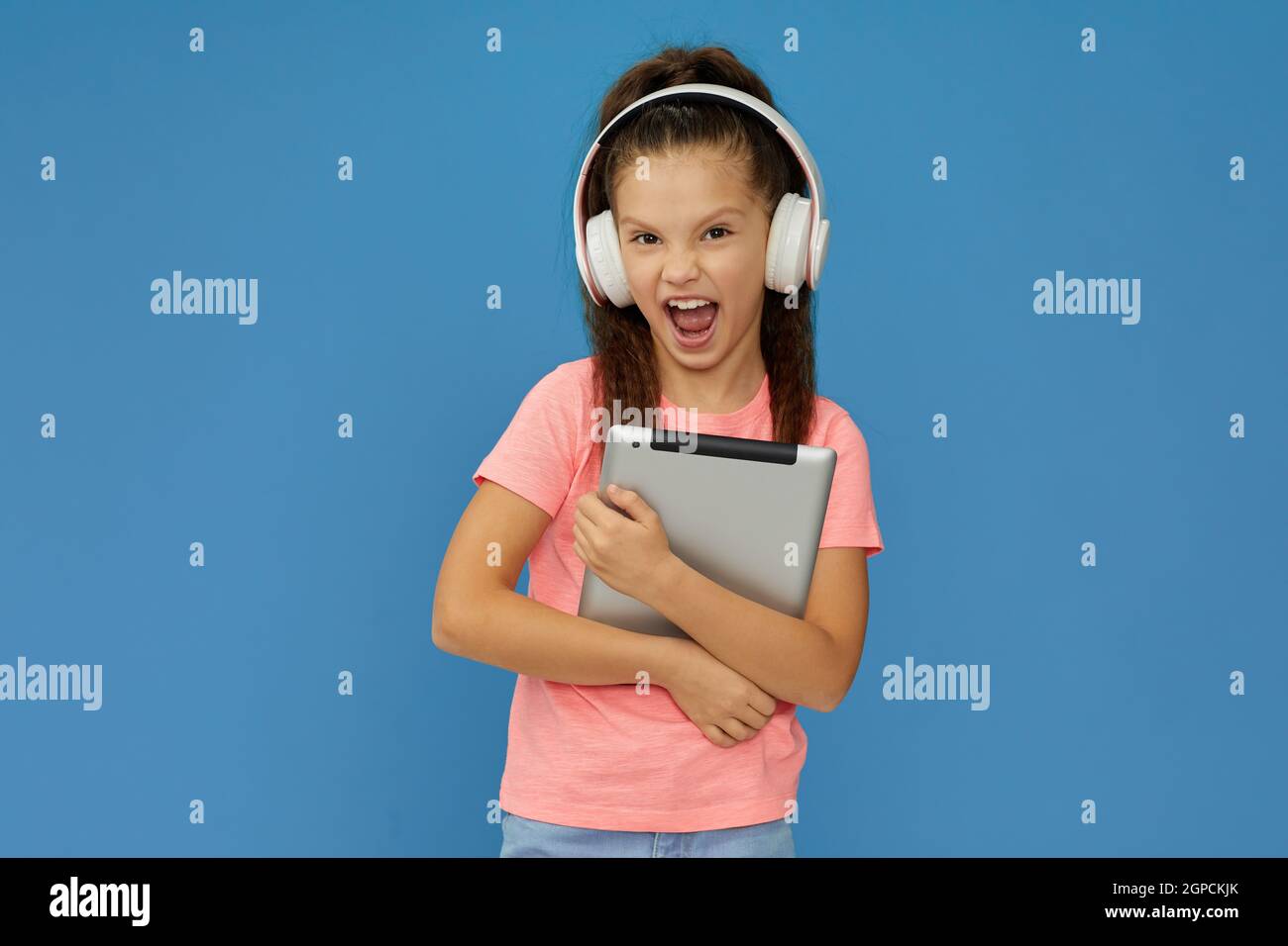 angry little child girl in headphones holding digital tablet and ...
