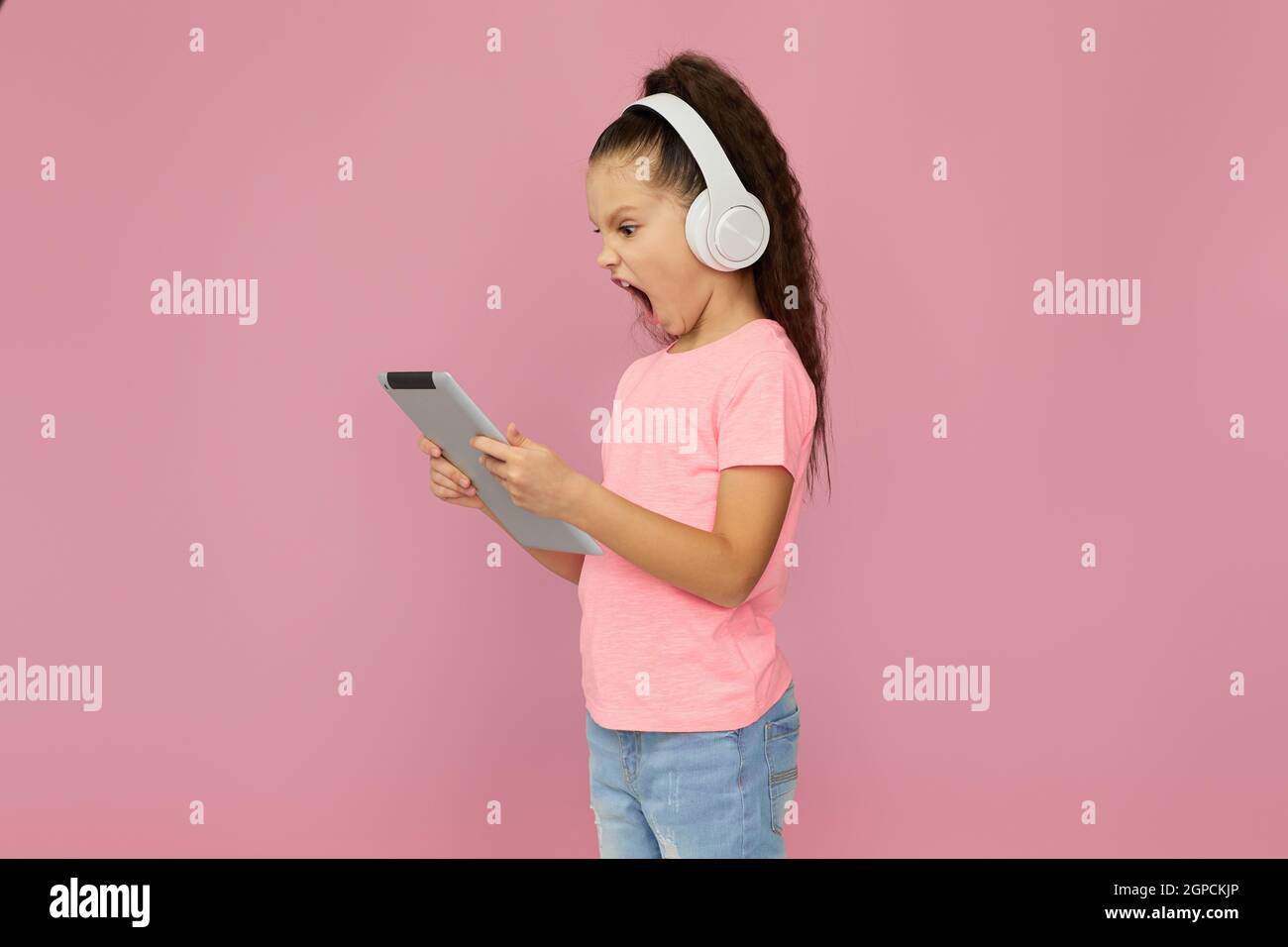 angry little child girl in headphones holding digital tablet and ...