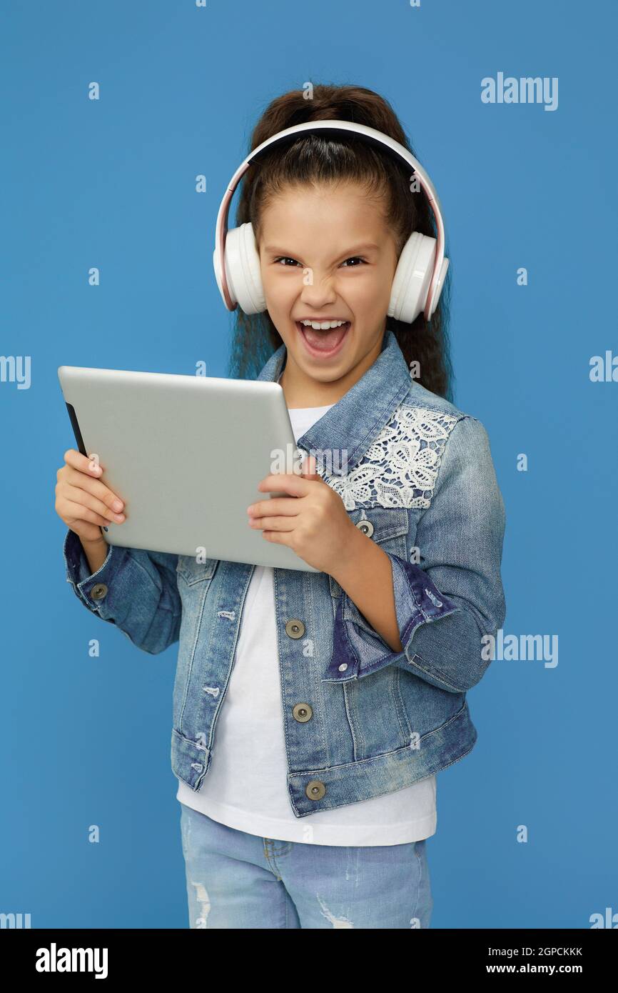 angry little child girl in white headphones holding digital tablet and ...