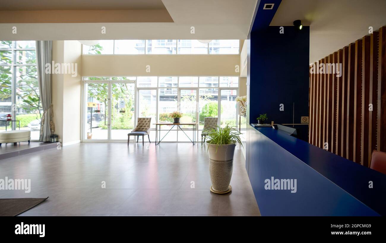 A long dark blue reception counter is located beside the hotel lobby ...
