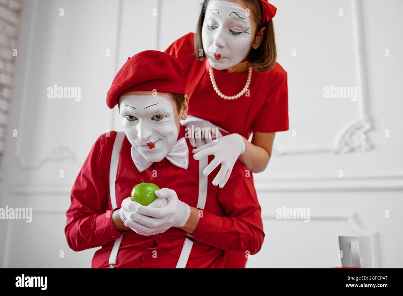 Two mime artists in red costumes, scene with apple. Pantomime theater ...