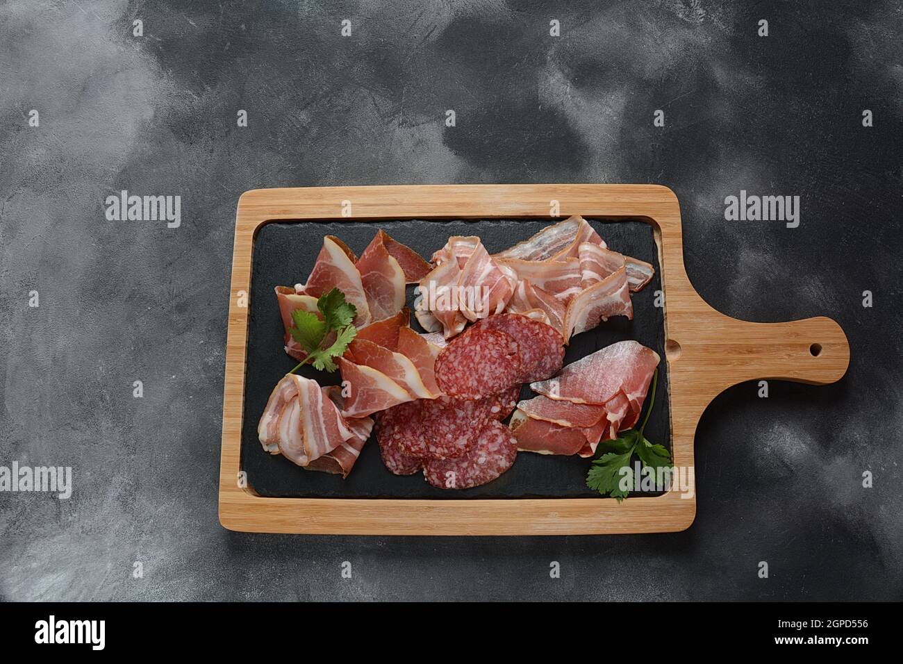 Salami, prosciutto, bacon on the cutting board. Delicatessen assortment ...