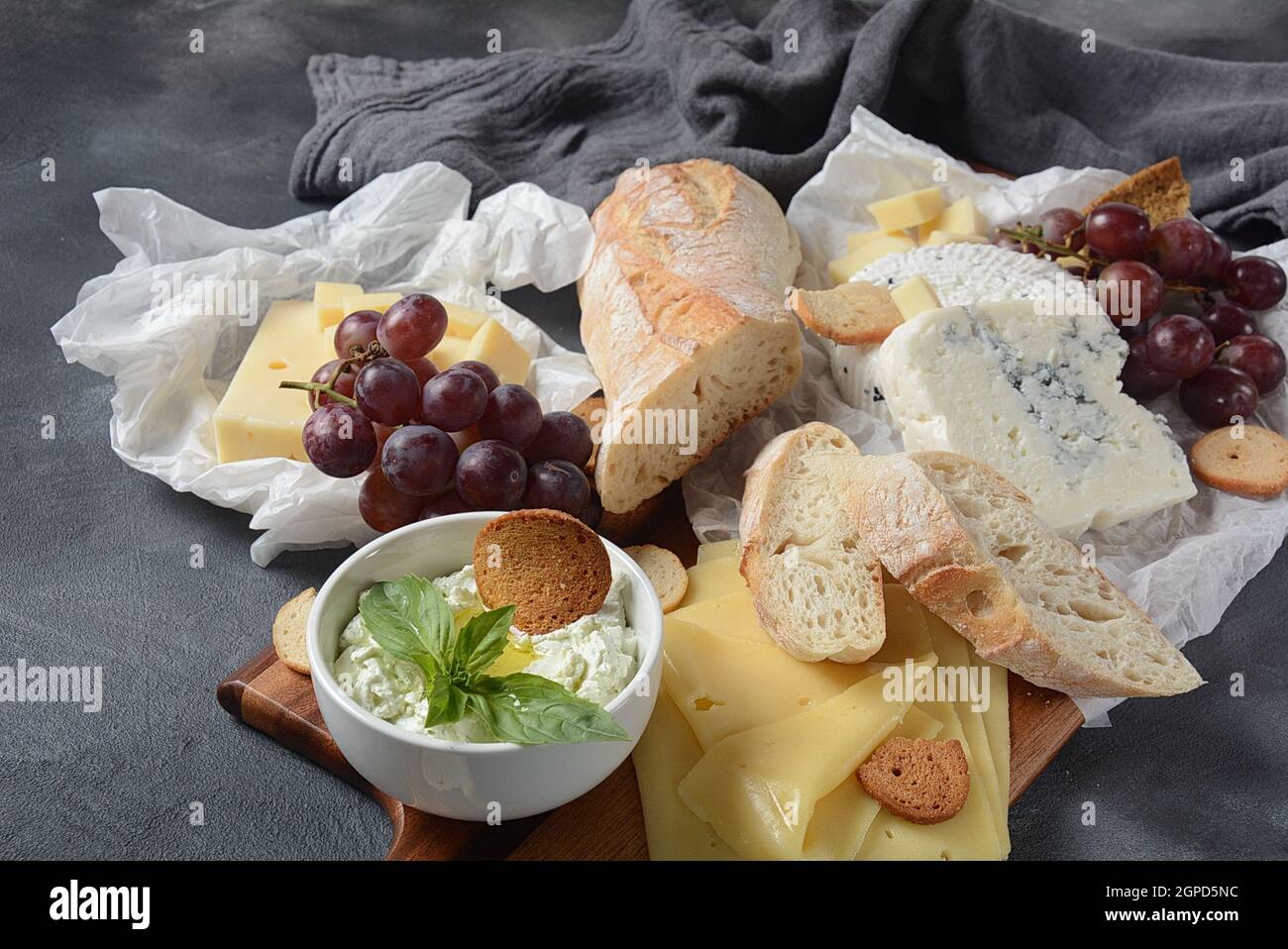 Cheese platter with assorted cheeses, grapes, snacks on dark background ...