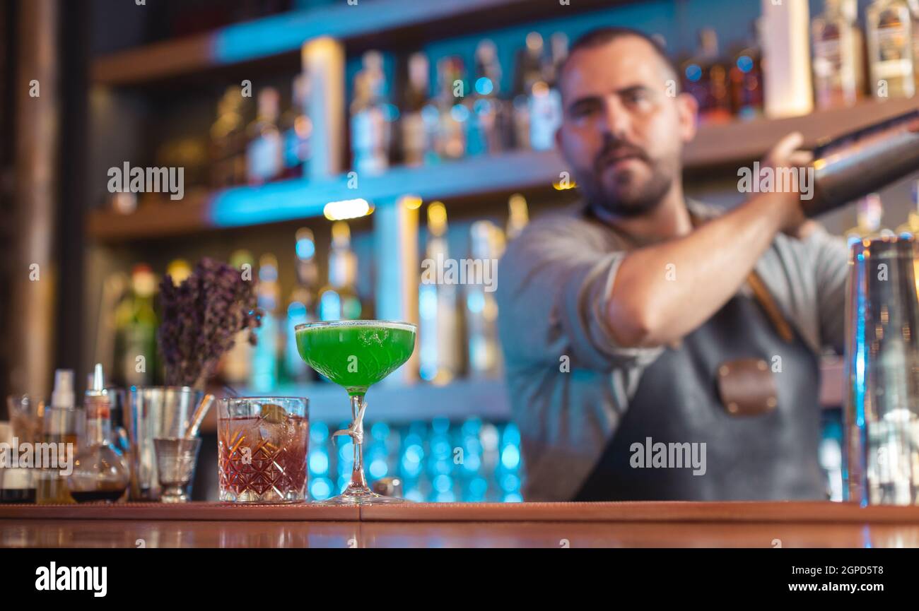 Young professional barman in bar interior shaking and mixing alcohol ...