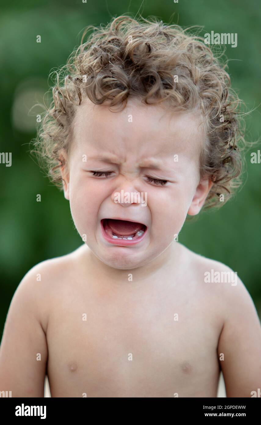 Sad baby with curly hair crying in the garden Stock Photo - Alamy