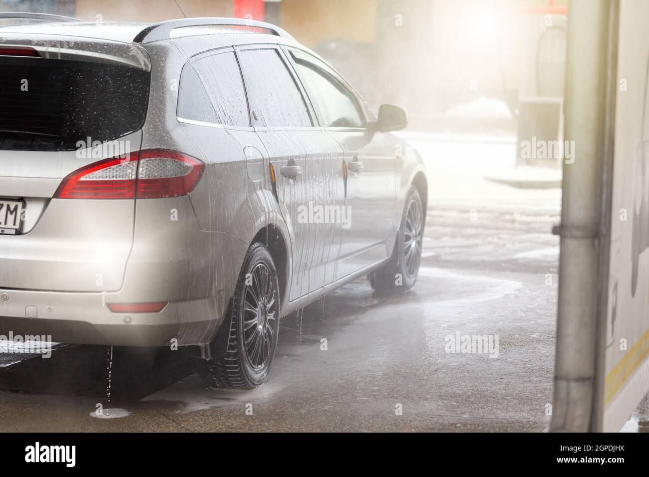 Rear view of a silver car being washed with water and soap in carwash ...