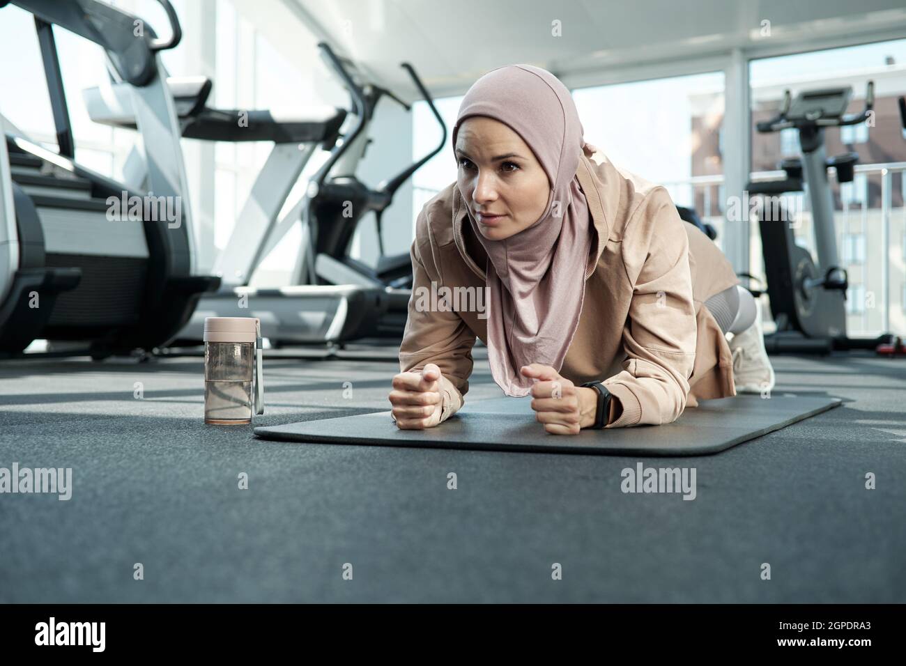 Horizontal portrait shot of sporty young adult Muslim woman wearing hijab doing strengthening ...