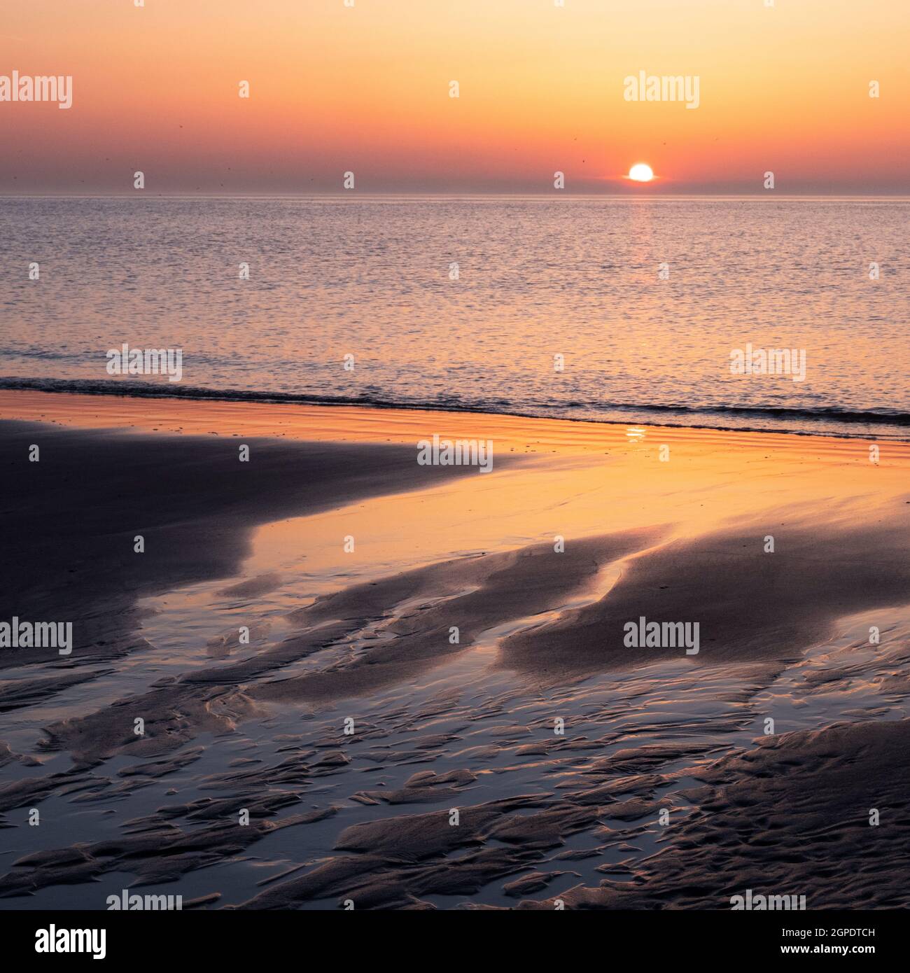 pattern in sand and colorful reflection of setting sun in water Stock ...