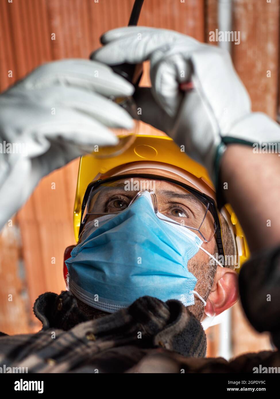 Electrician worker at work replaces the light bulb protected by helmet ...
