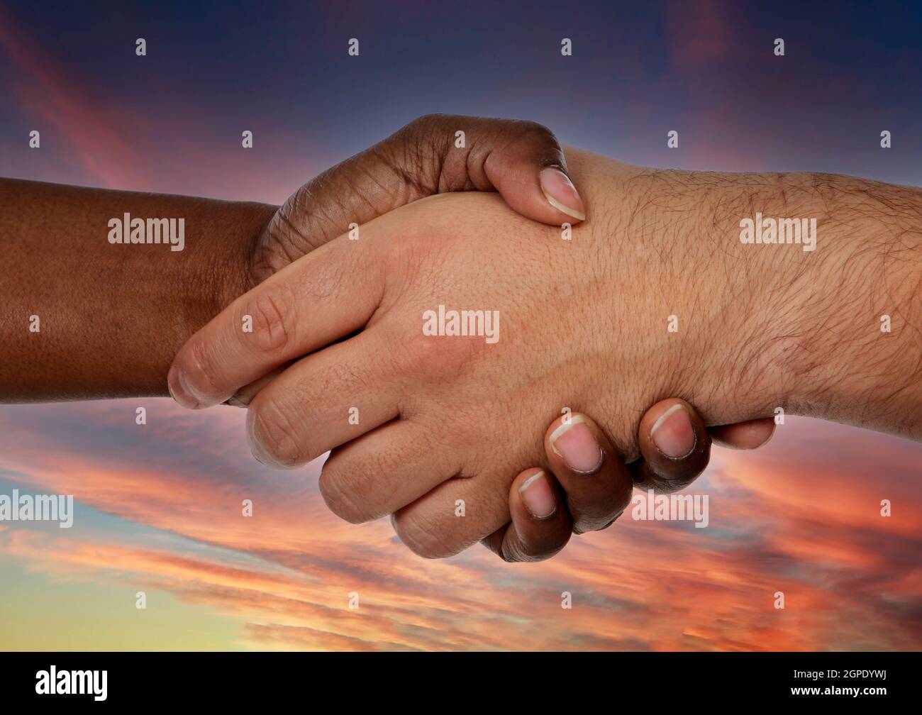 Handshake between two hands with different colors on a amazing sky of ...