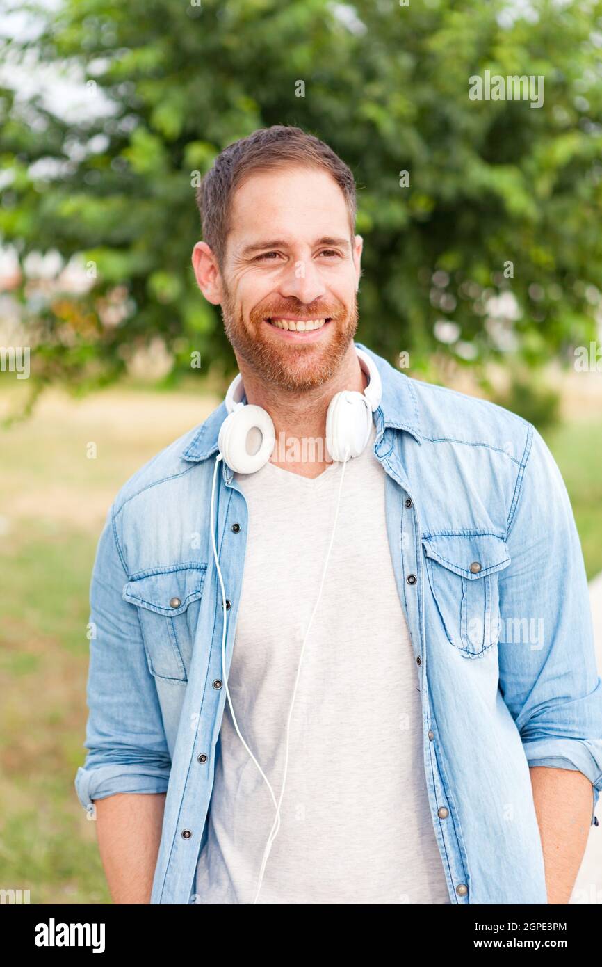 Casual guy with white headphones is taking a walk in the park in his ...