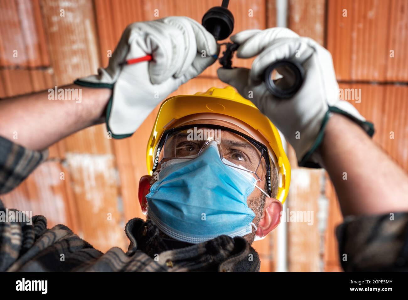 Electrician worker at work replaces the lamp holder protected by helmet ...