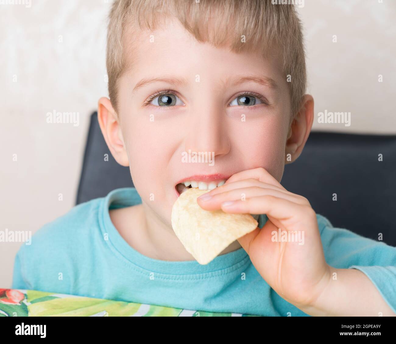 A child with pleasure eating potato chips sitting at a table on a light ...