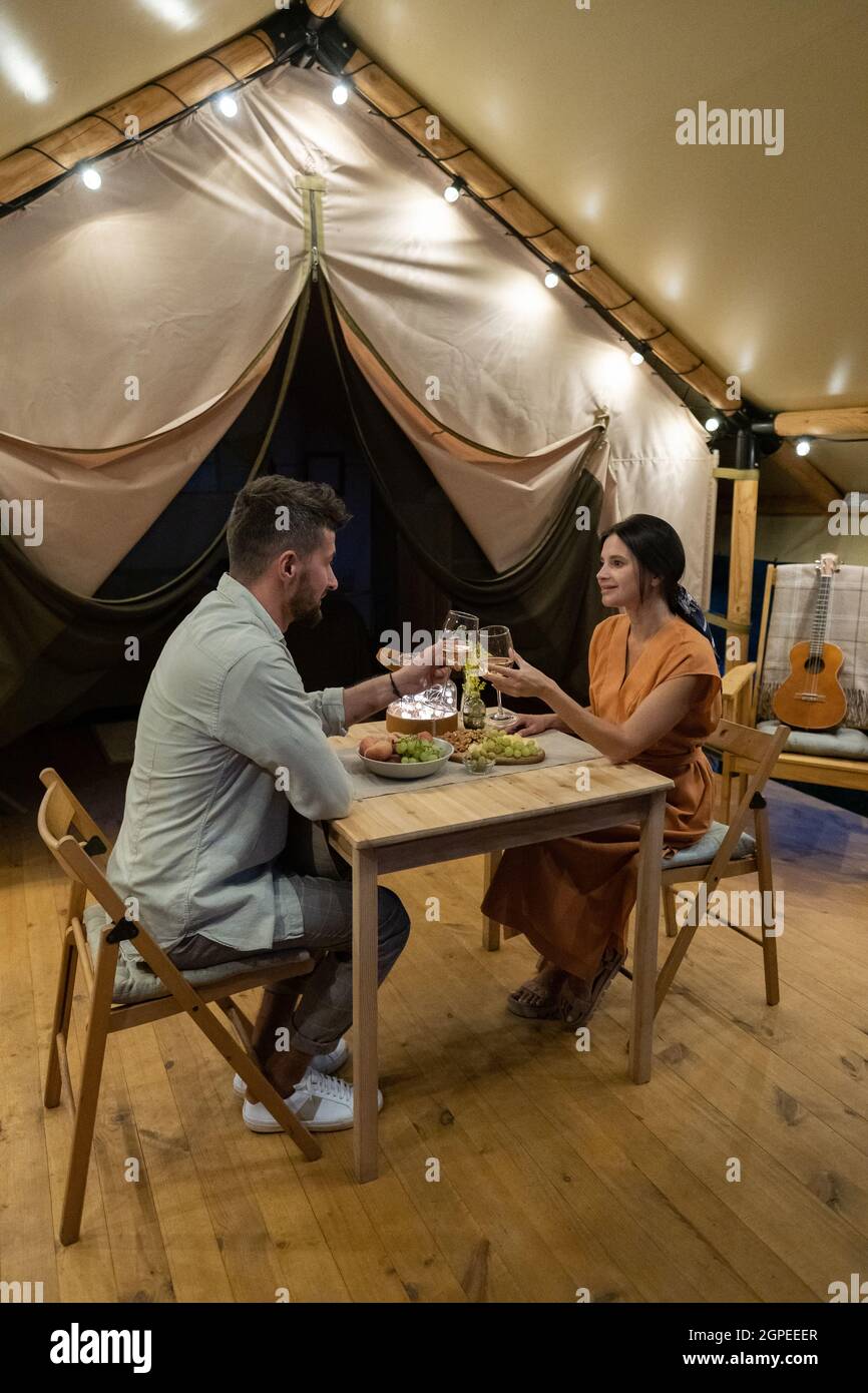 Young amorous couple cheering up with glasses of wine over served table ...