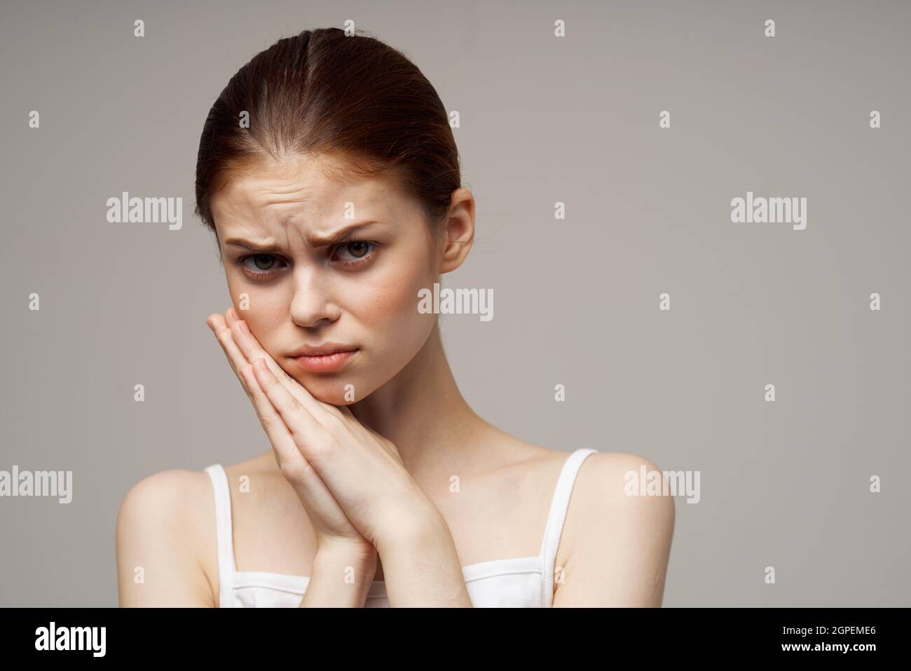 disgruntled woman holding on to face pain in teeth light background ...