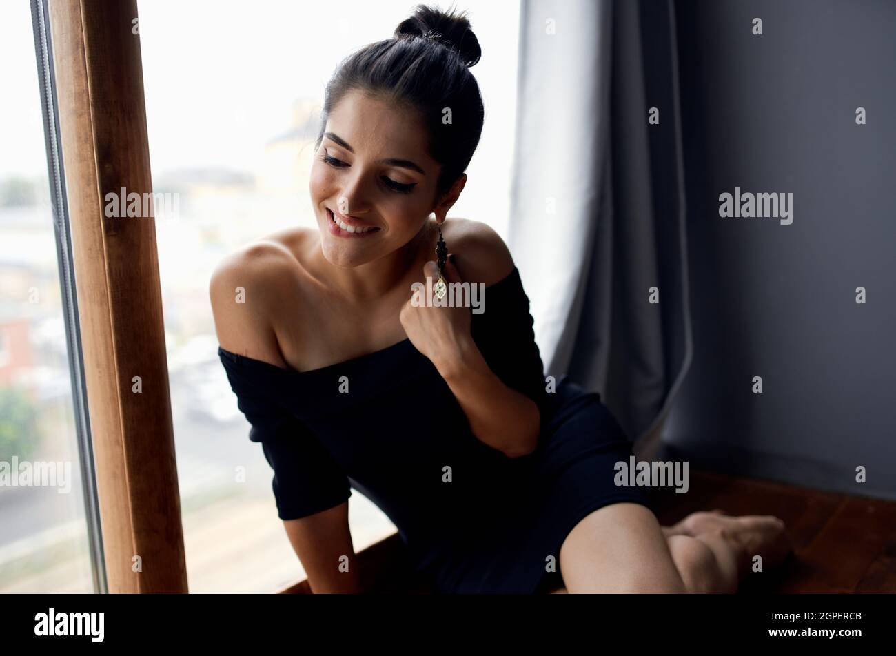 pretty woman in a black dress near the window posing lifestyle studio ...