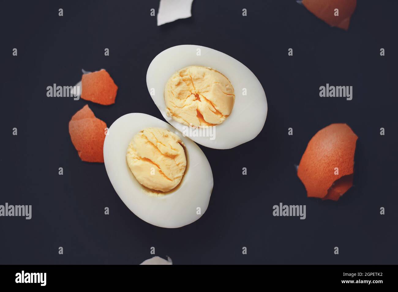 The halves of a peeled boiled egg lie on a dark background next to a ...