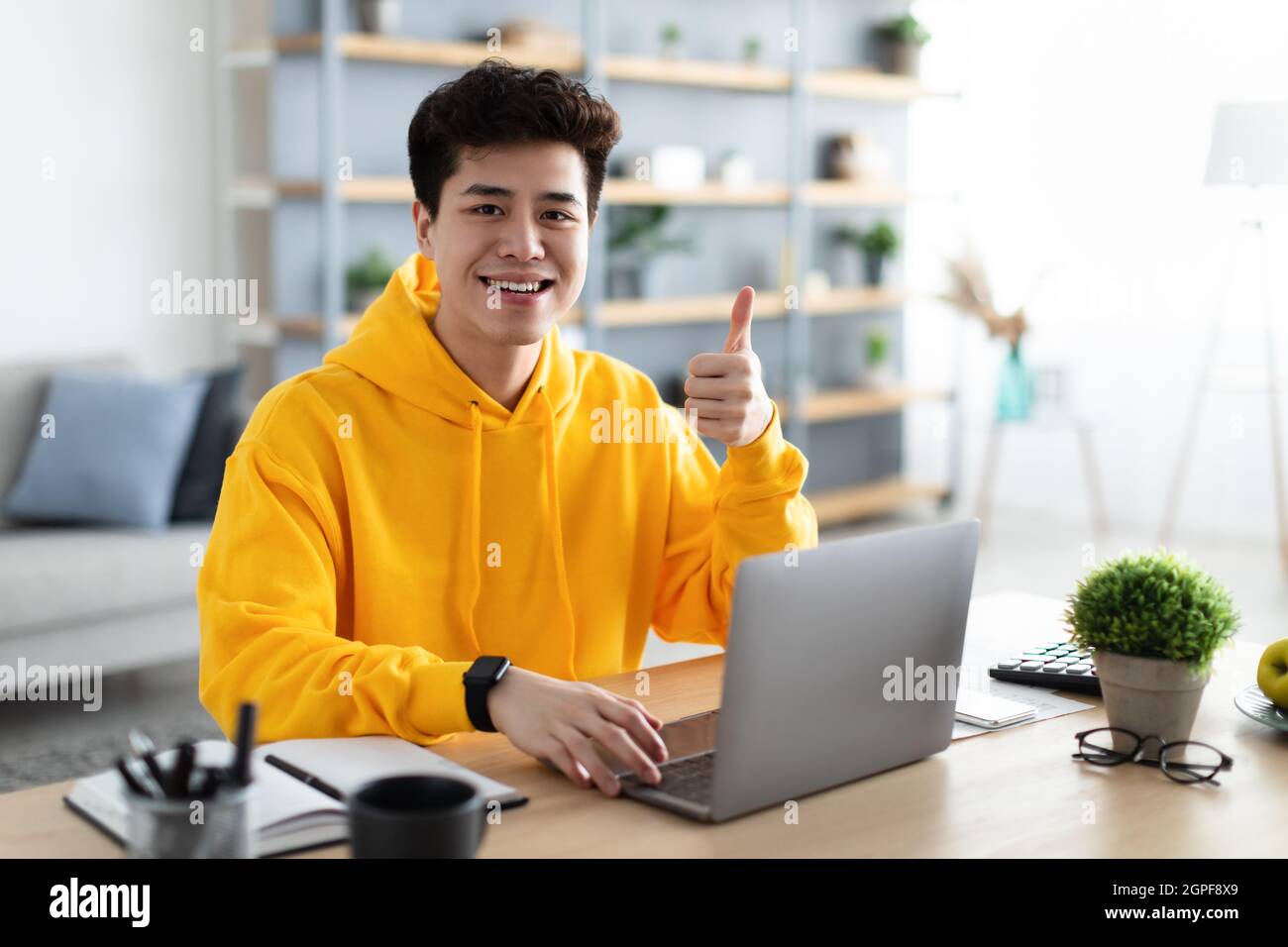 Smiling asian man working on laptop showing thumbs up Stock Photo - Alamy