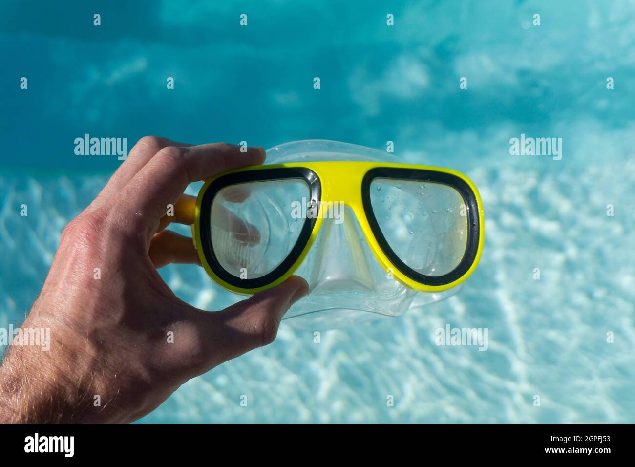 Yellow swimming goggles next to a clear blue rippled swimming pool ...