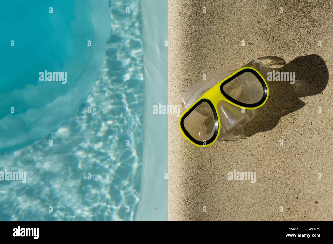 Yellow swimming goggles next to a clear blue rippled swimming pool ...