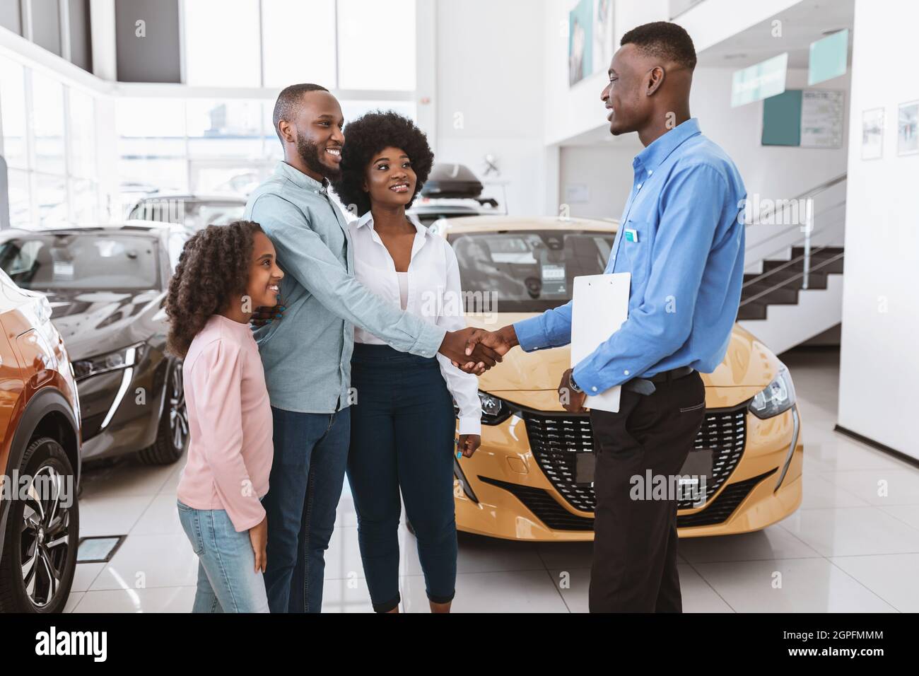 Friendly salesman shaking hands with Afro family, making car purchase ...