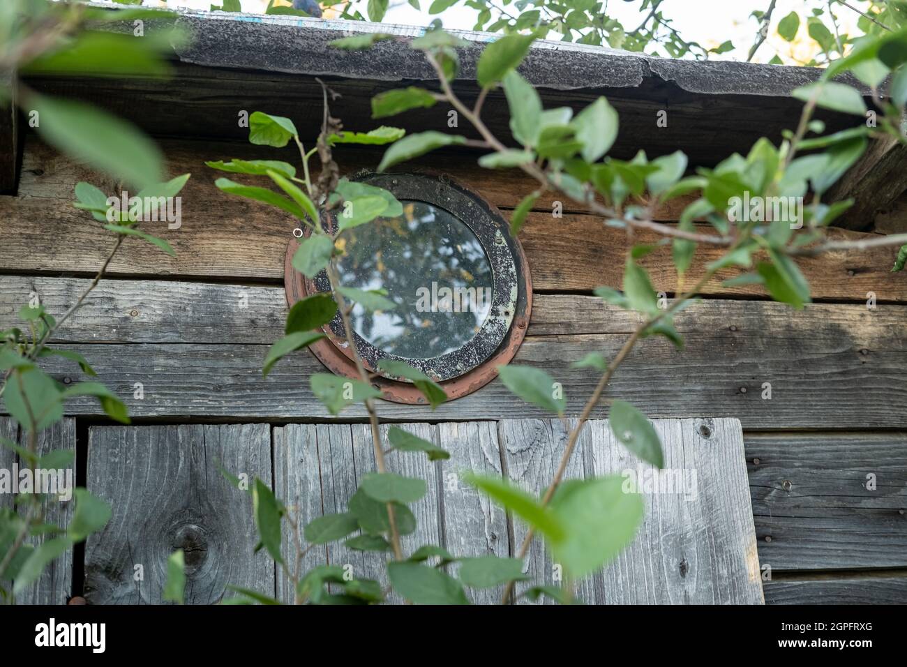 Round window under the roof of an old wooden shed or toilet, in a ...