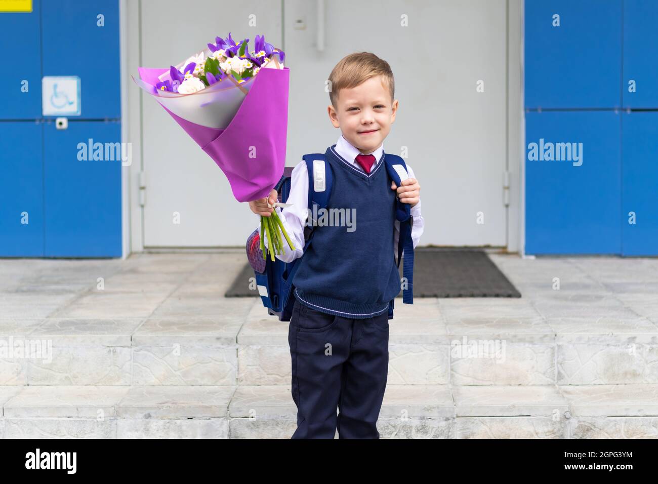 A cute first-grader boy in a school uniform with a beautiful bouquet of ...