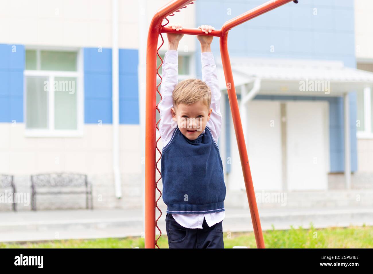 A cute first grader boy at the school on the playground hangs on a ...