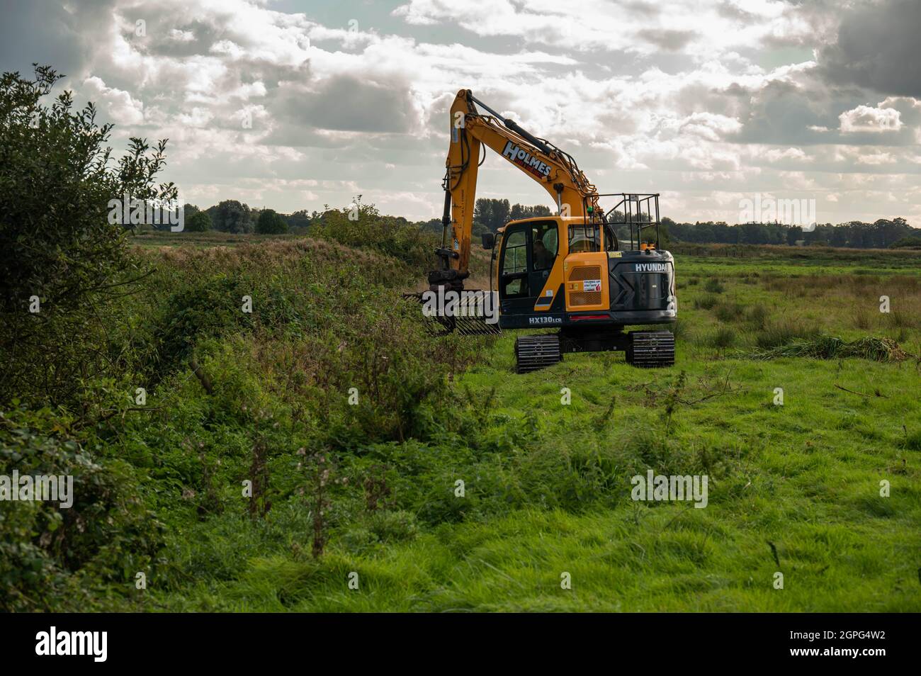 A digger maintaining drainage ditches on low-lying grazing marsh on the ...