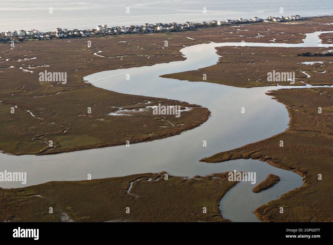 Aerial view of a thin strip of homes surrounded by salt marsh and the ...