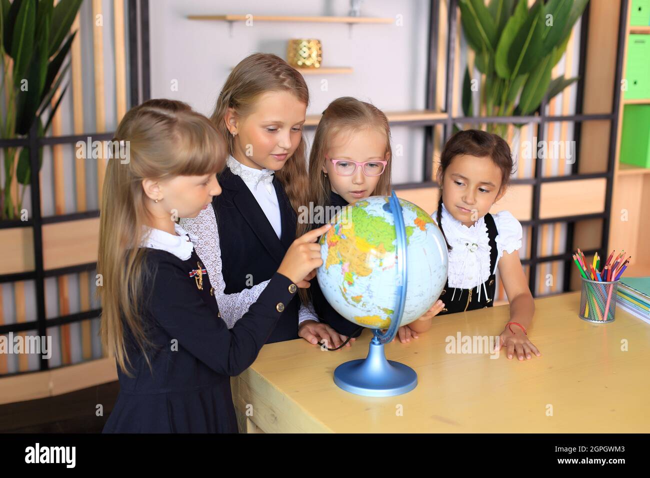 Children in school uniforms with a globe in the office. Girls in the ...