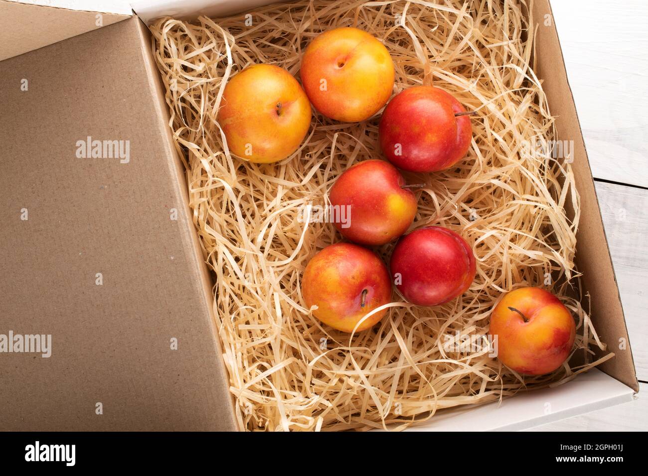 Several juicy sweet yellow-red plums in a box with shavings, close-up ...