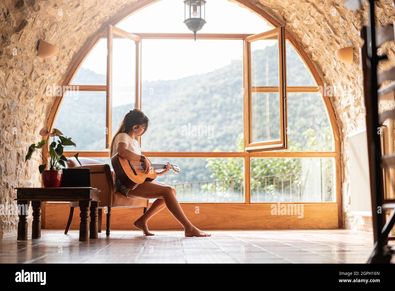 Singing woman playing Spanish guitar next to a window in a large room ...