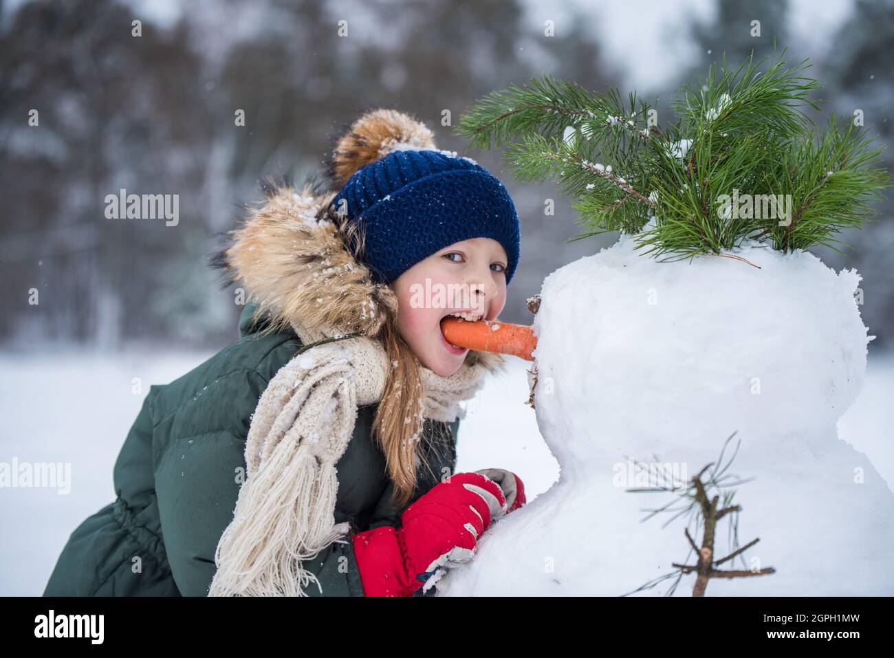 Blonde cute girl happy child eating snowman carrot nose Stock Photo - Alamy
