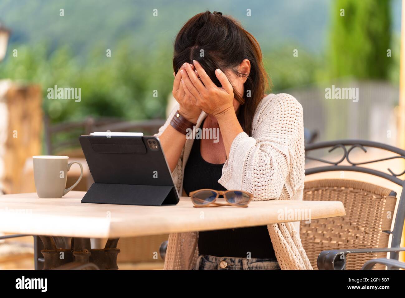 Sad woman crying at a table on a terrace outdoors with a tablet Stock ...