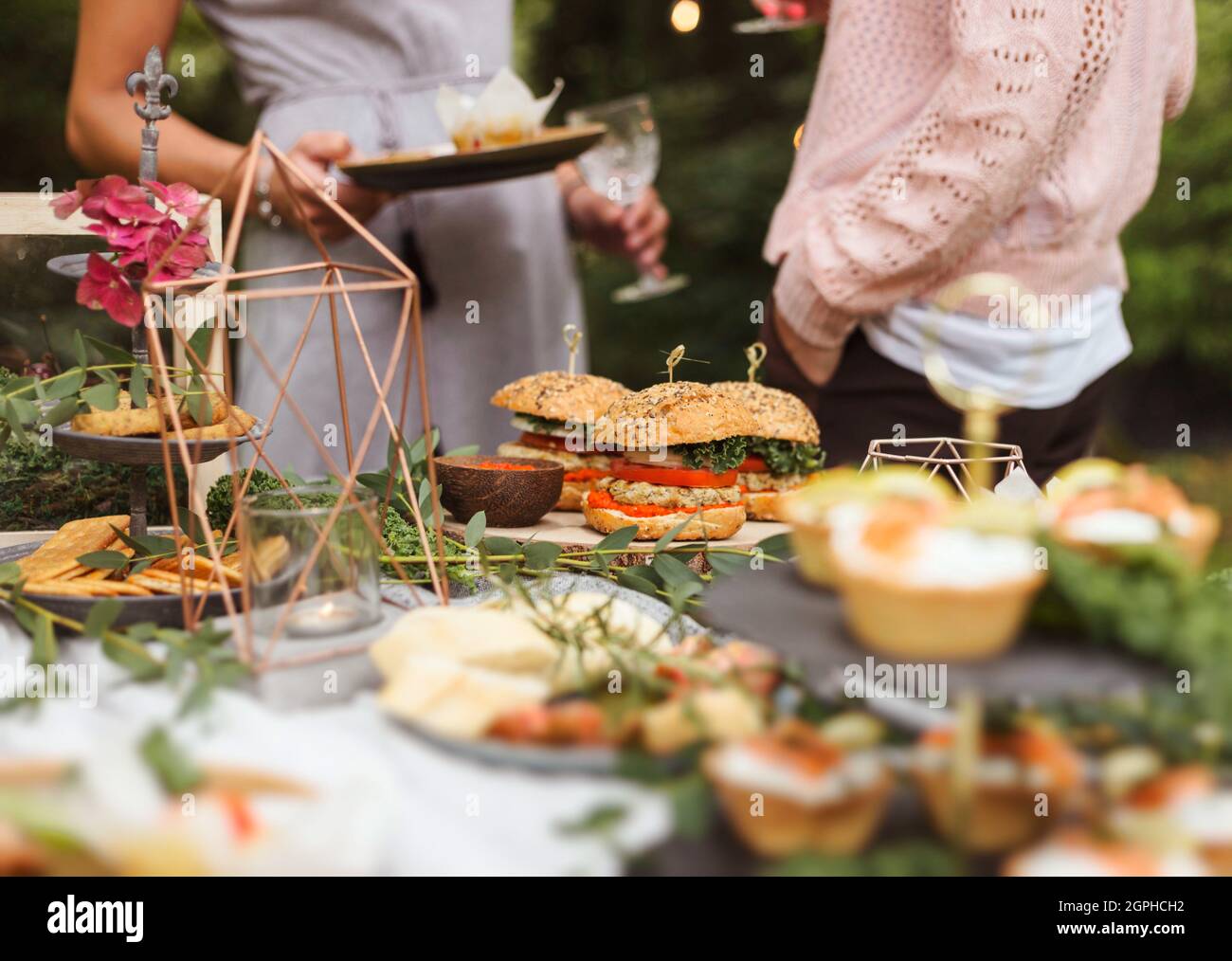 Anonymous female guests holding plates and drinksat informal garden ...