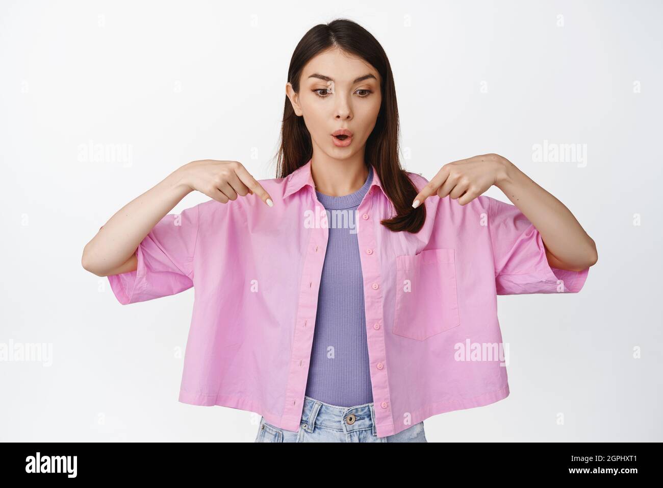 Surprised girl points and looks down with amazed face expression ...