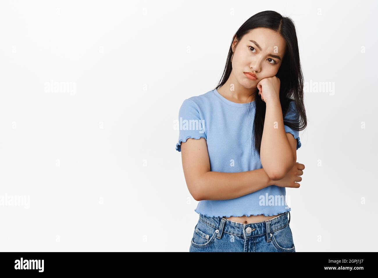 Angry asian girl lean on fist, looking aside with pissed-off moody face ...