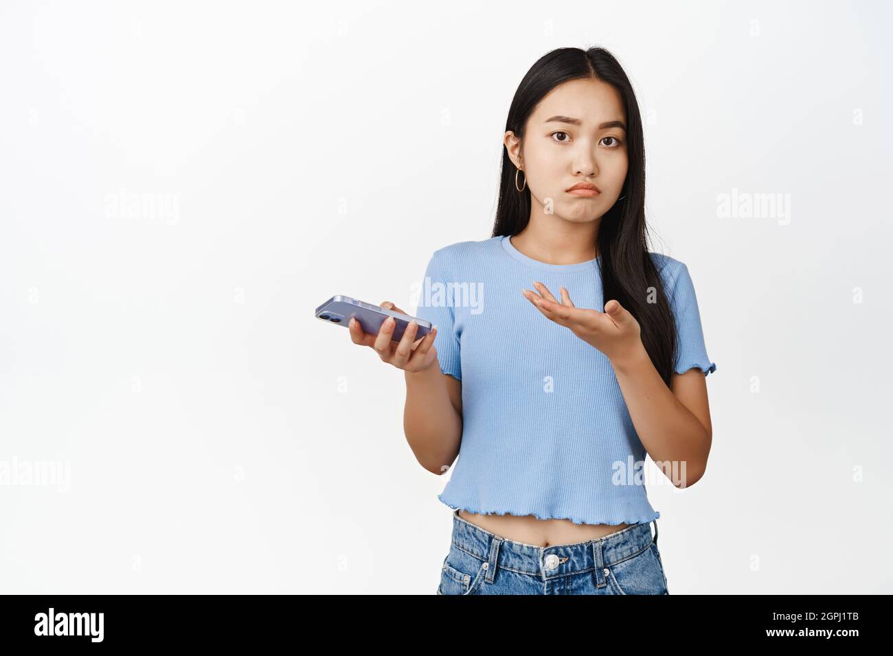 Young asian girl pointing at her phone with confused face, looking ...