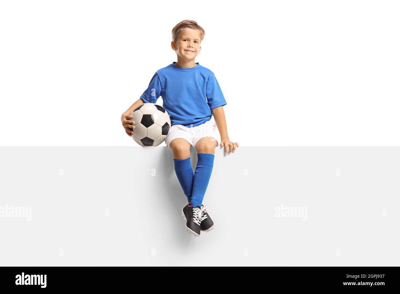 Cute little boy in a blue soccer jersey sitting on a blank panel and ...