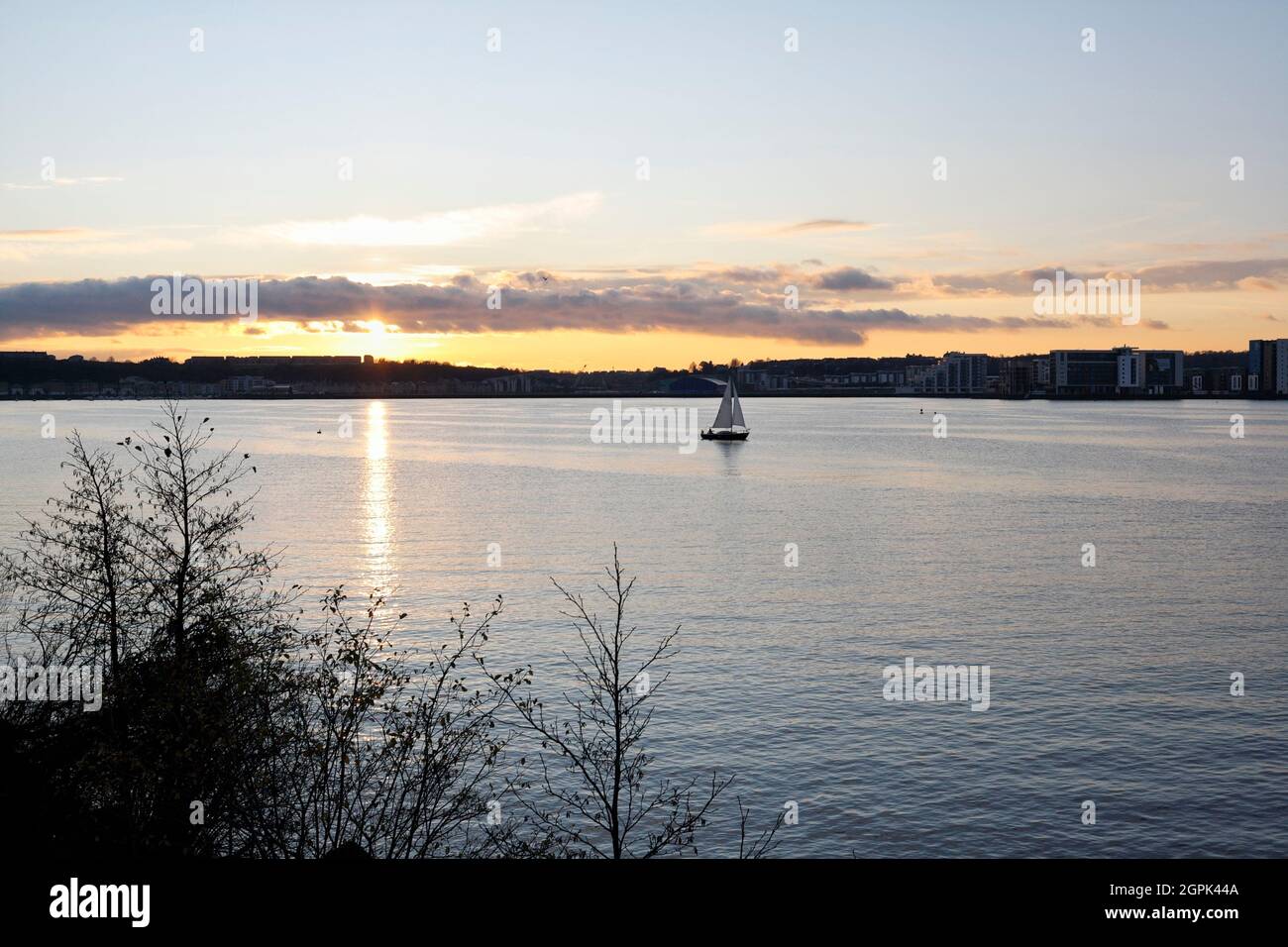 A lone sailing yacht on the Cardiff Bay Barrage lake against a sunset ...