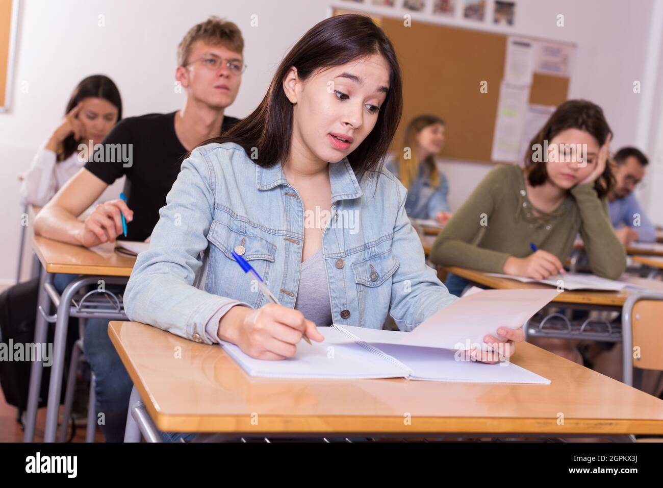 Young girl is writing test and thinking about questions at the desk ...