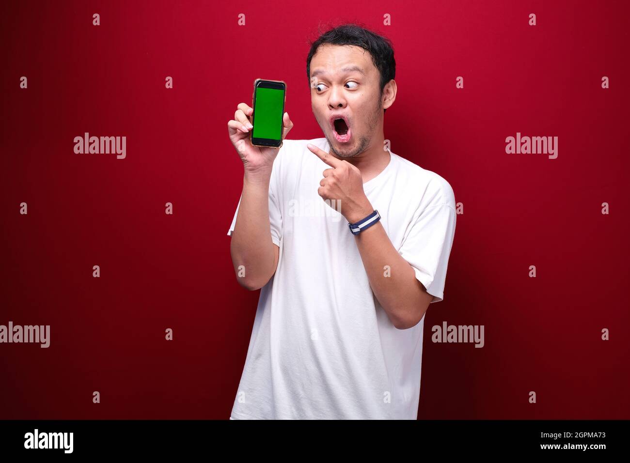 Shock Young Asian man pointing on green blank space on smartphone on ...