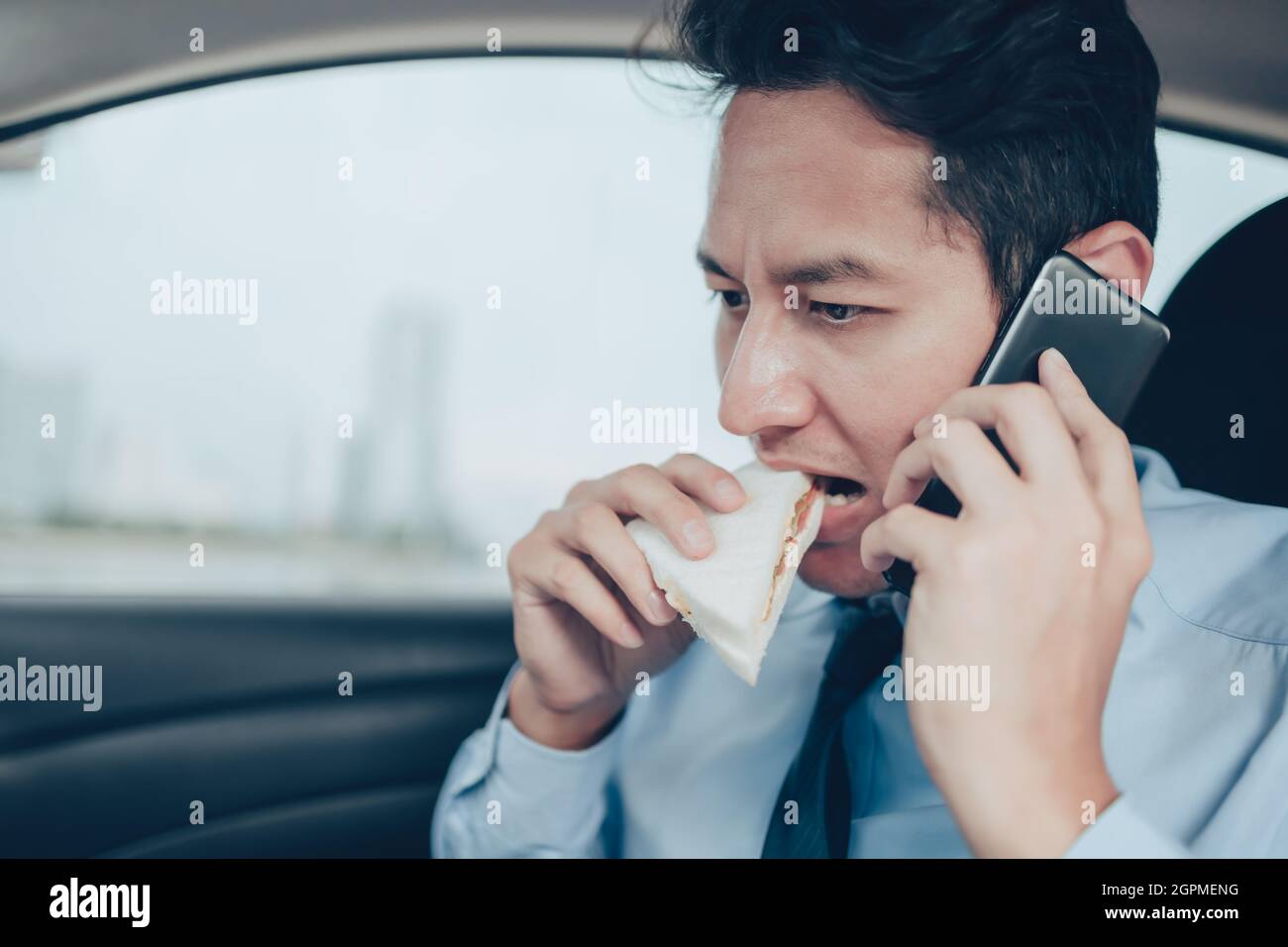 Businessman eating sandwich while talking on the phone in the drivers ...