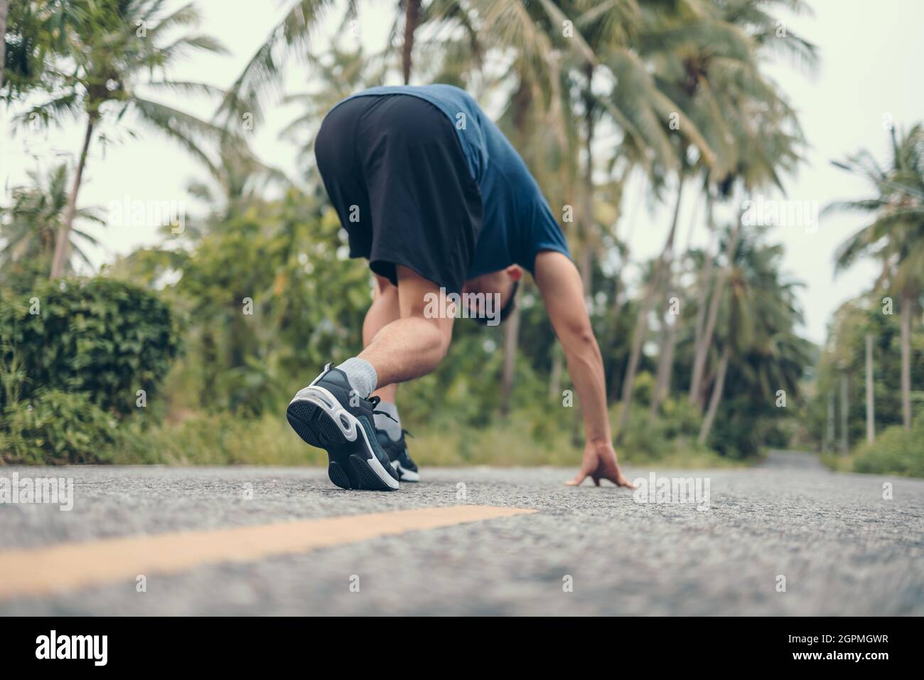 Athlete man in running start pose on the road in the forest. Start and ...