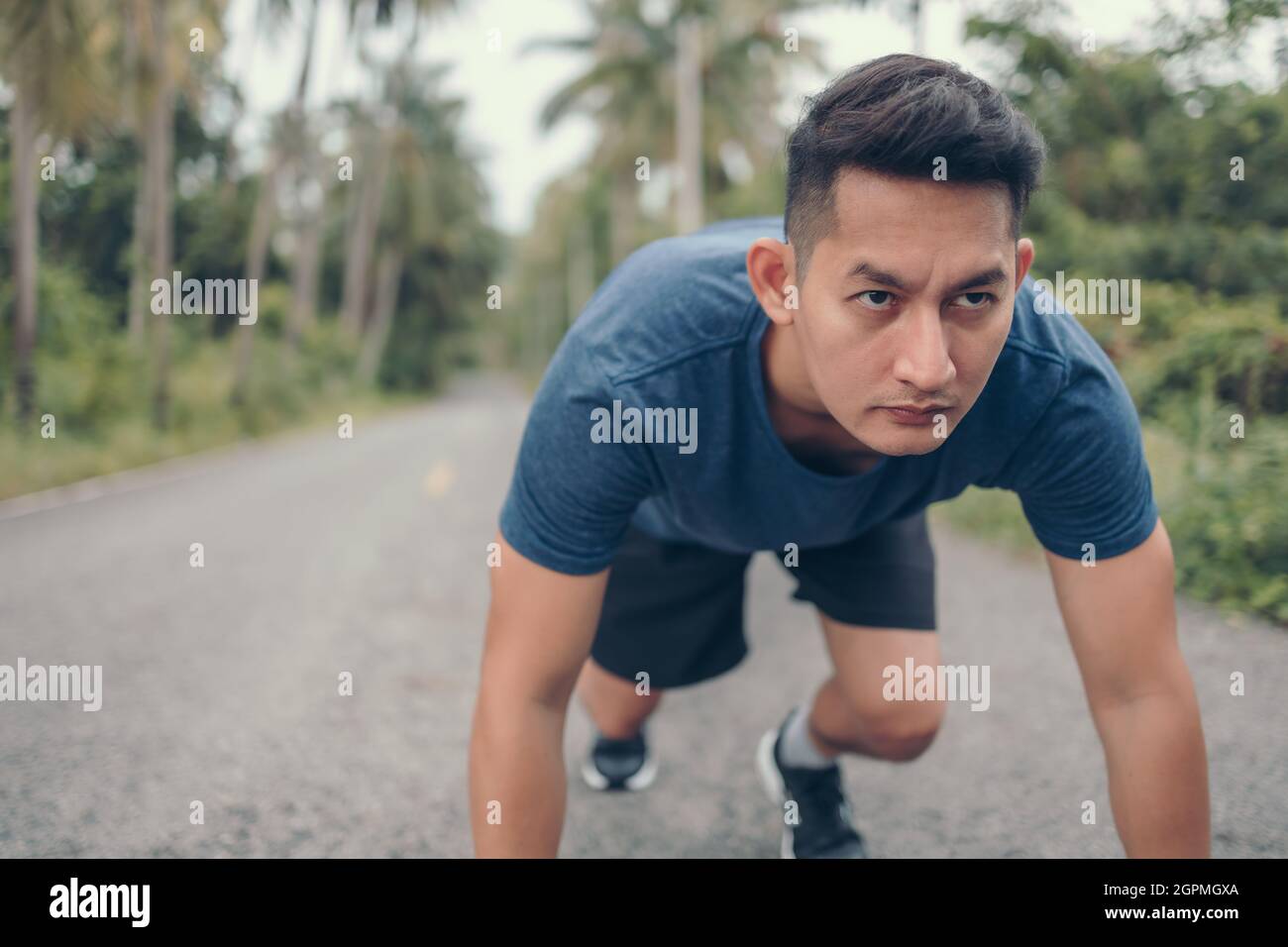 Athlete man in running start pose on the road in the forest. Start and ...