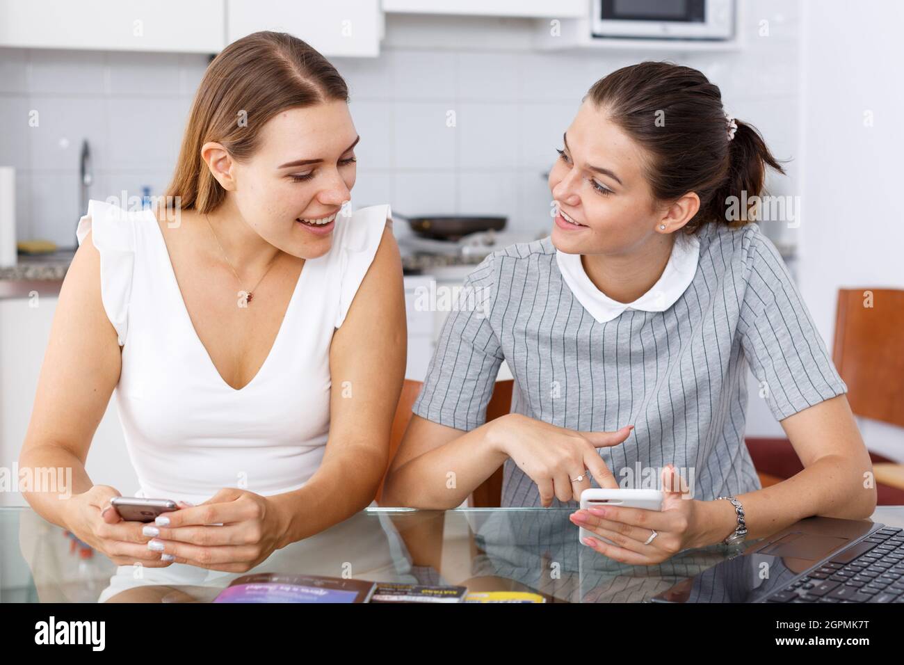 Young smiling girlfriends using phones and chatting table Stock Photo ...