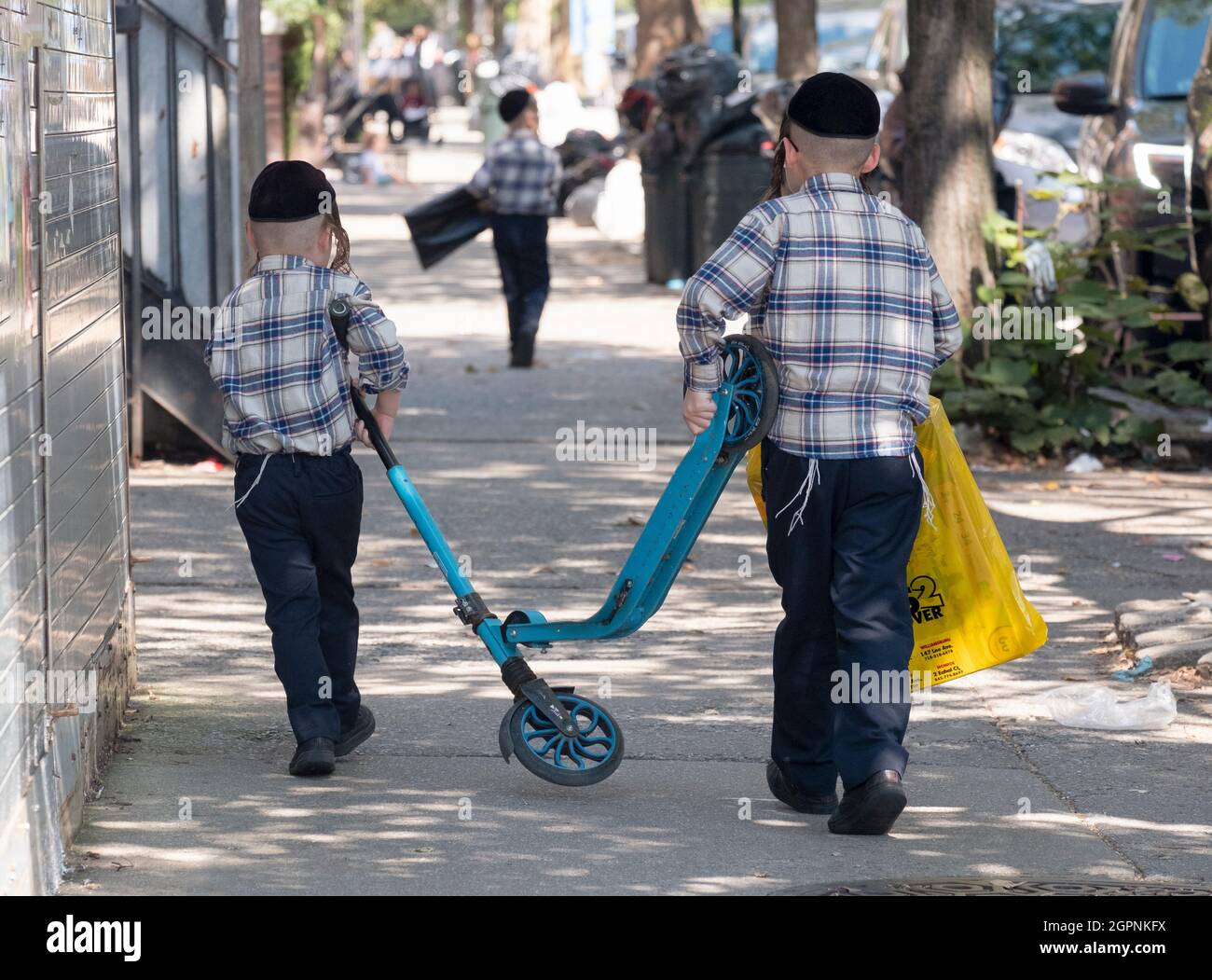 Orthodox Jewish brothers dressed alike carry their scooter home in an ...